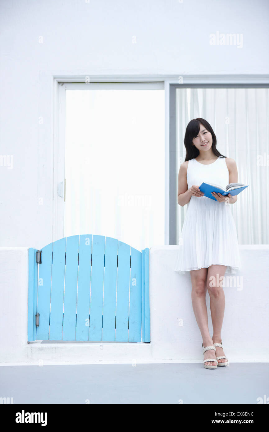 A woman reading a book leaning on a white fence Stock Photo - Alamy