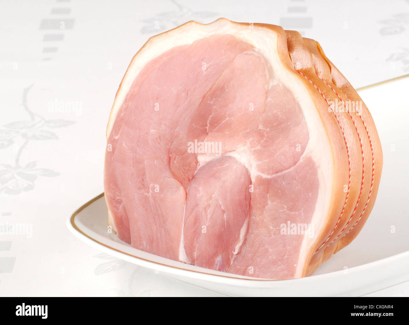 an uncooked joint of smoked gammon on a white plate and tablecloth ...
