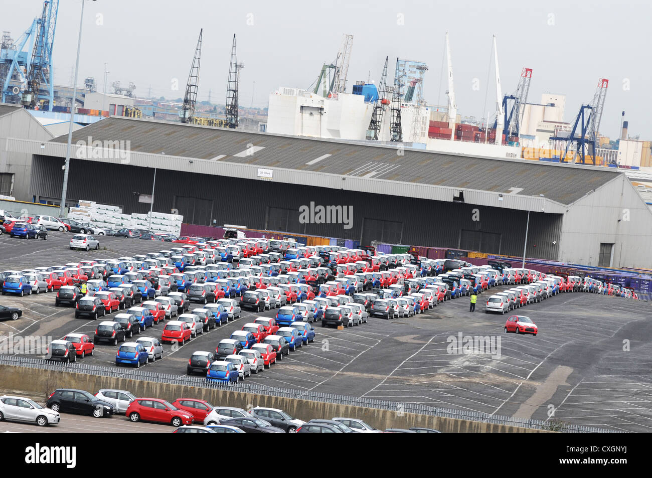 Newly imported multicoloured cars in car park at dock with cranes ...