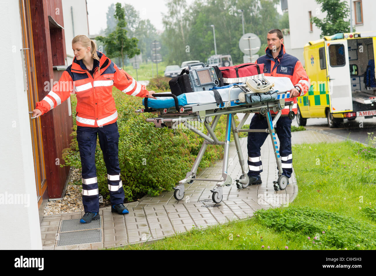 Paramedics carrying emergency stretcher ambulance house call visit door ...