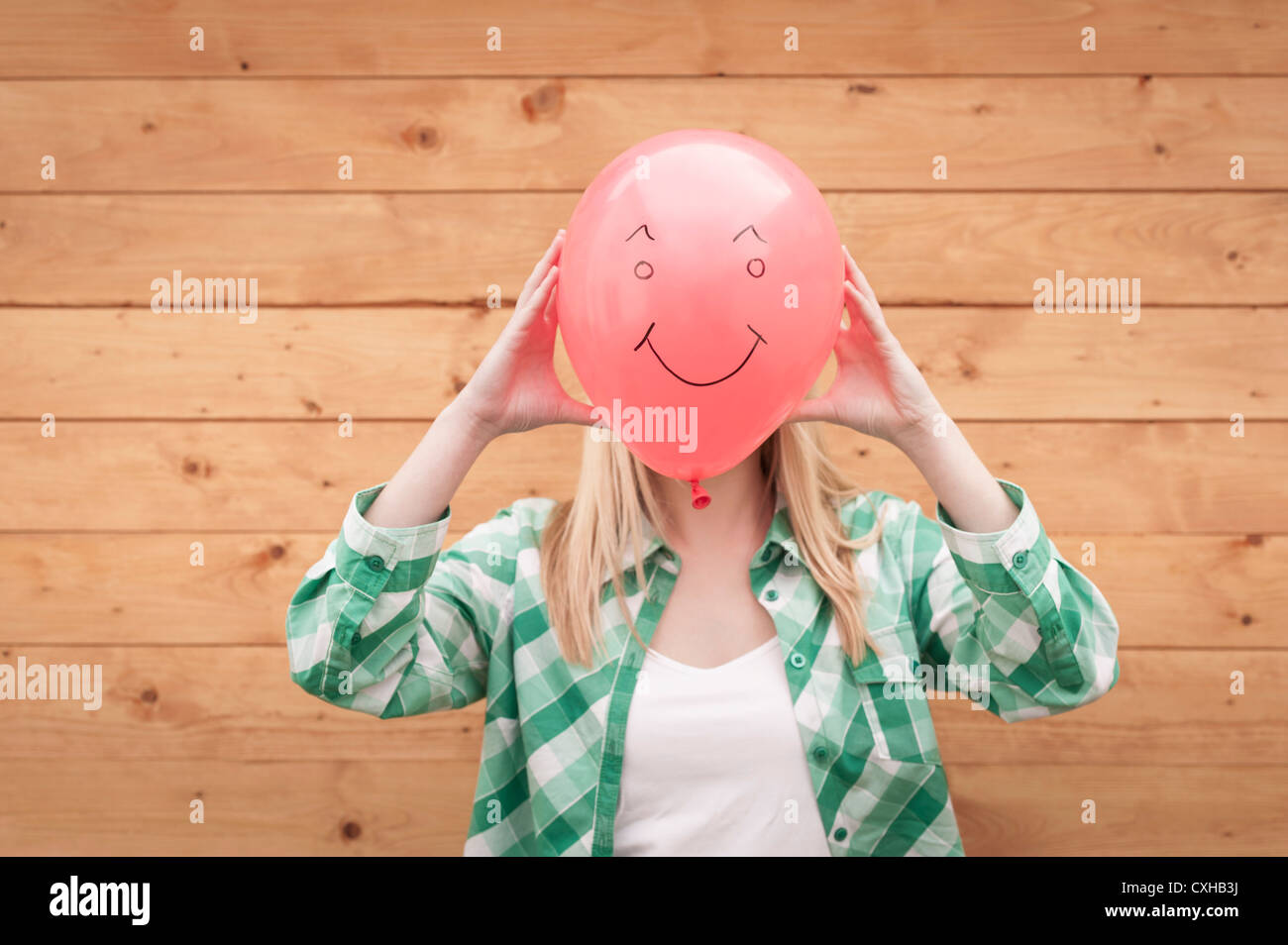 Germany, North Rhine Westphalia, Teenage girl covering face with smiley ...