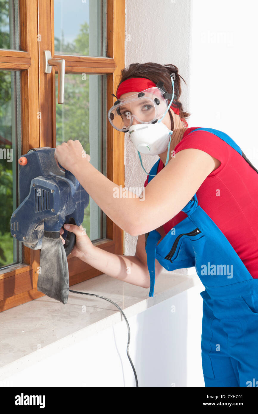 Germany, Bavaria, Young woman working with electric planer, portrait ...