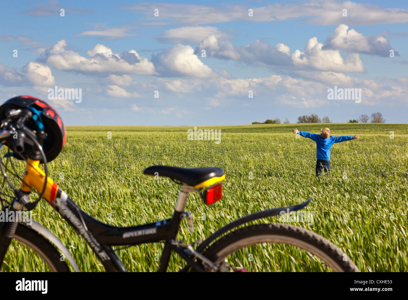 Germany, Hamburg, Boy standing and stretching arms in field, bicycle in ...