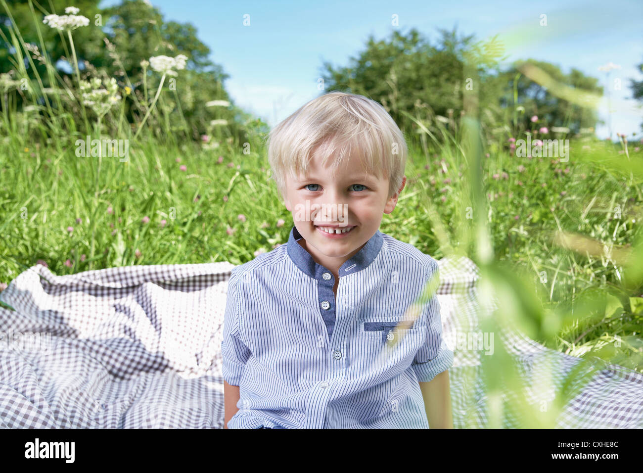 Germany, Cologne, Boy sitting on blanket in meadow, smiling, portrait ...
