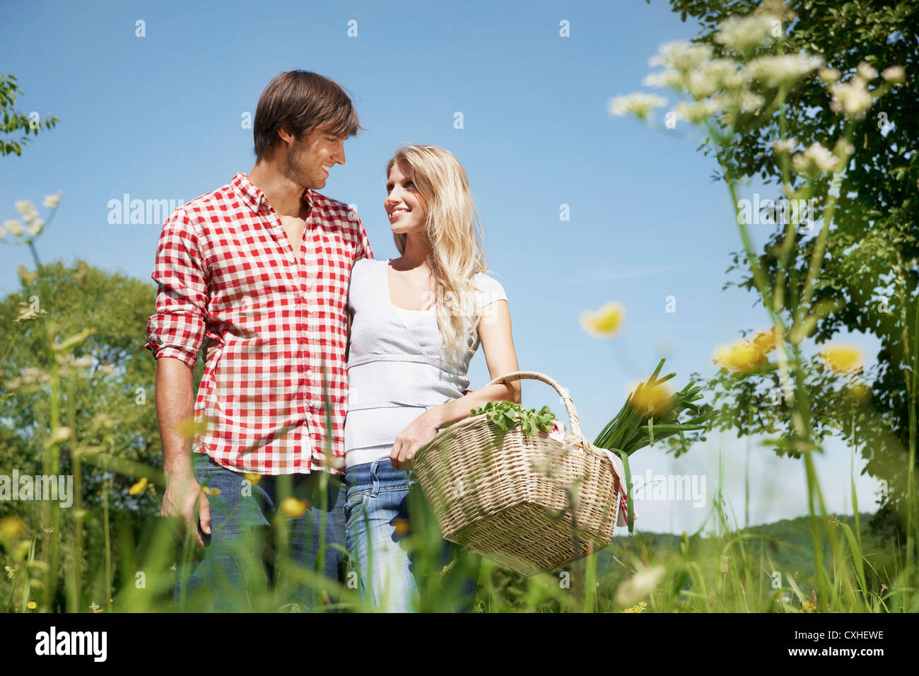 Germany, Cologne, Young couple with picnic basket in meadow, smiling ...