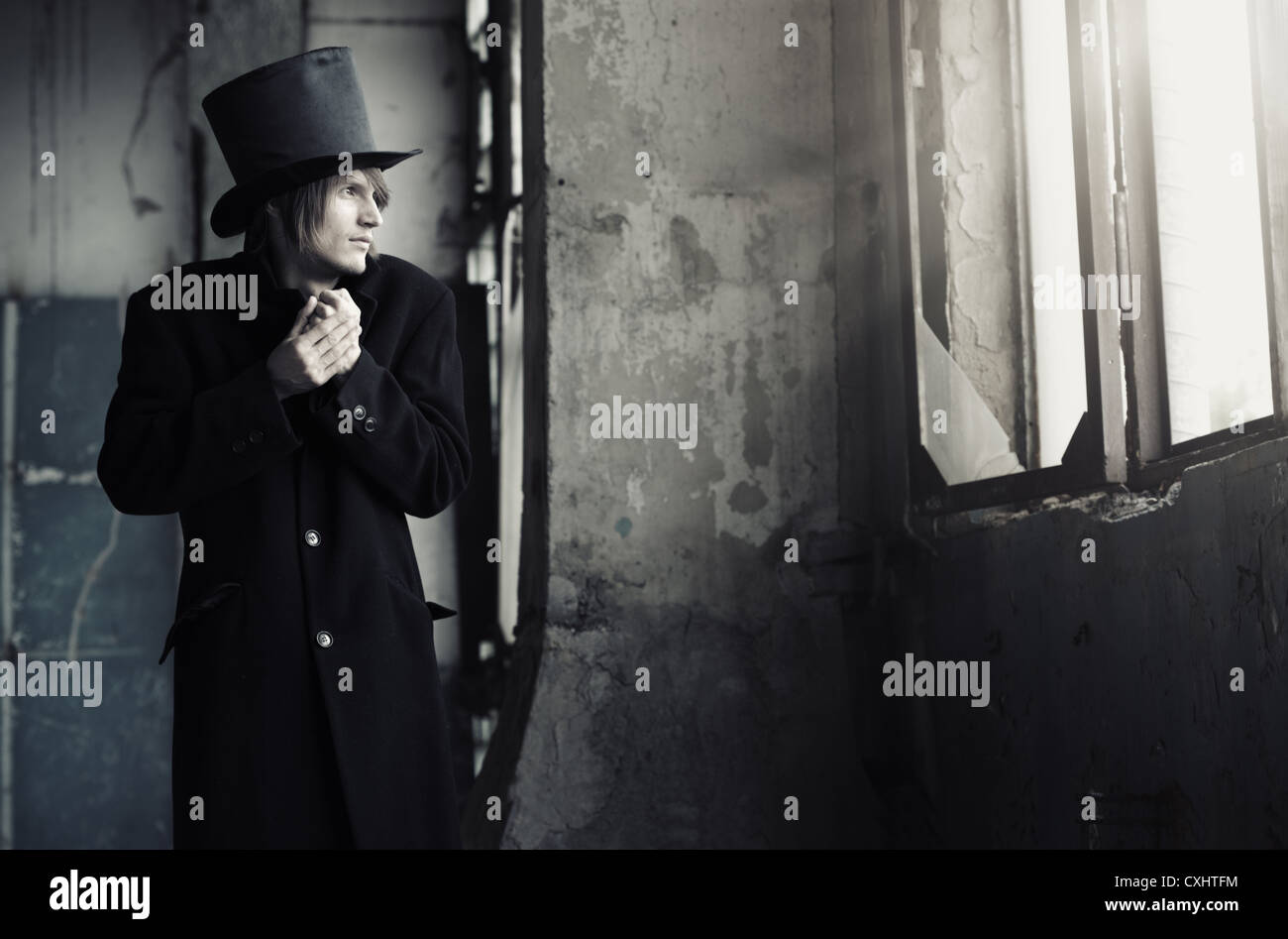 Man in black vintage coat and top-hat hiding in the old ruined interior ...