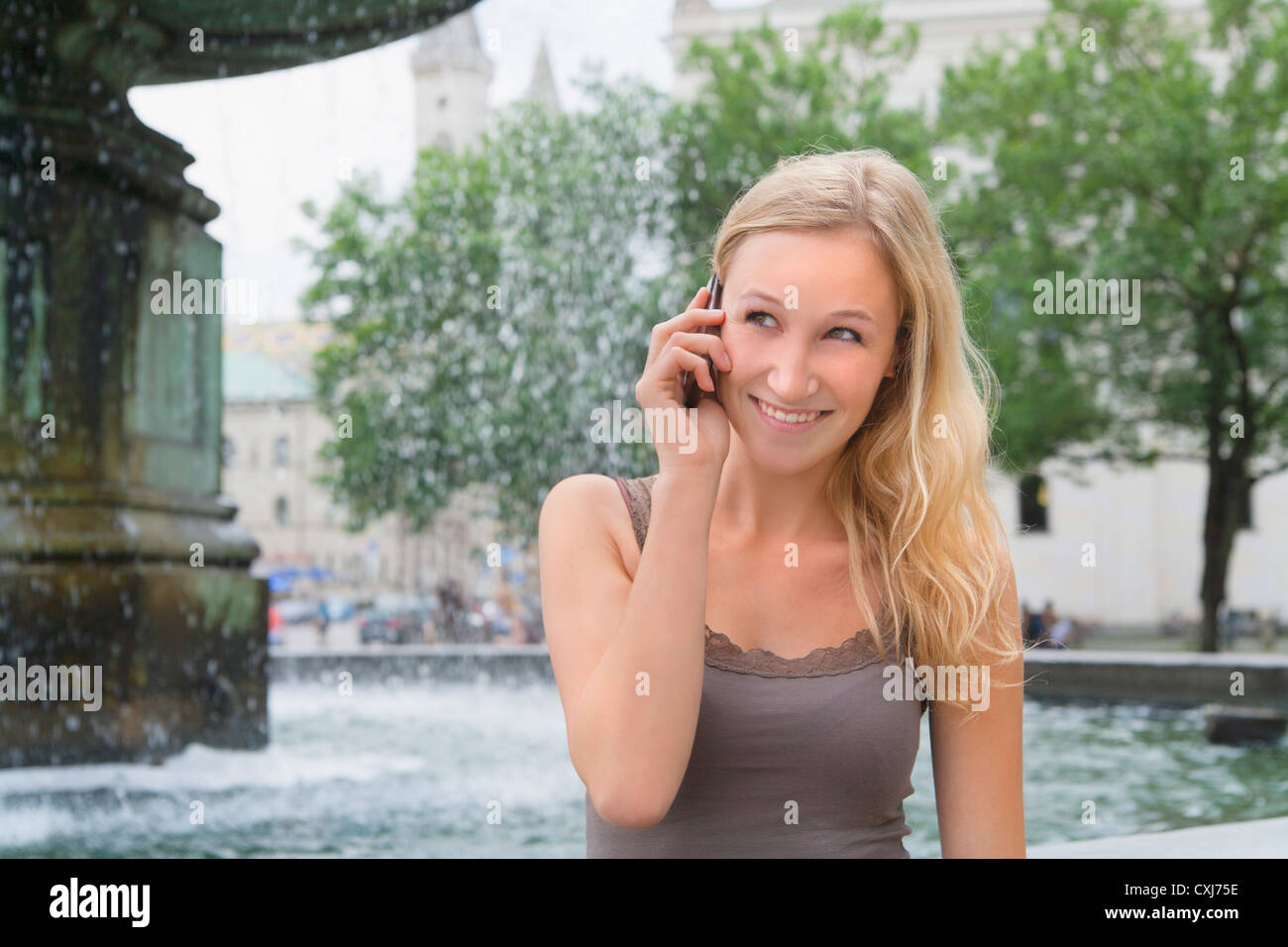 Germany, Bavaria, Munich, Young woman talking on phone in front of ...