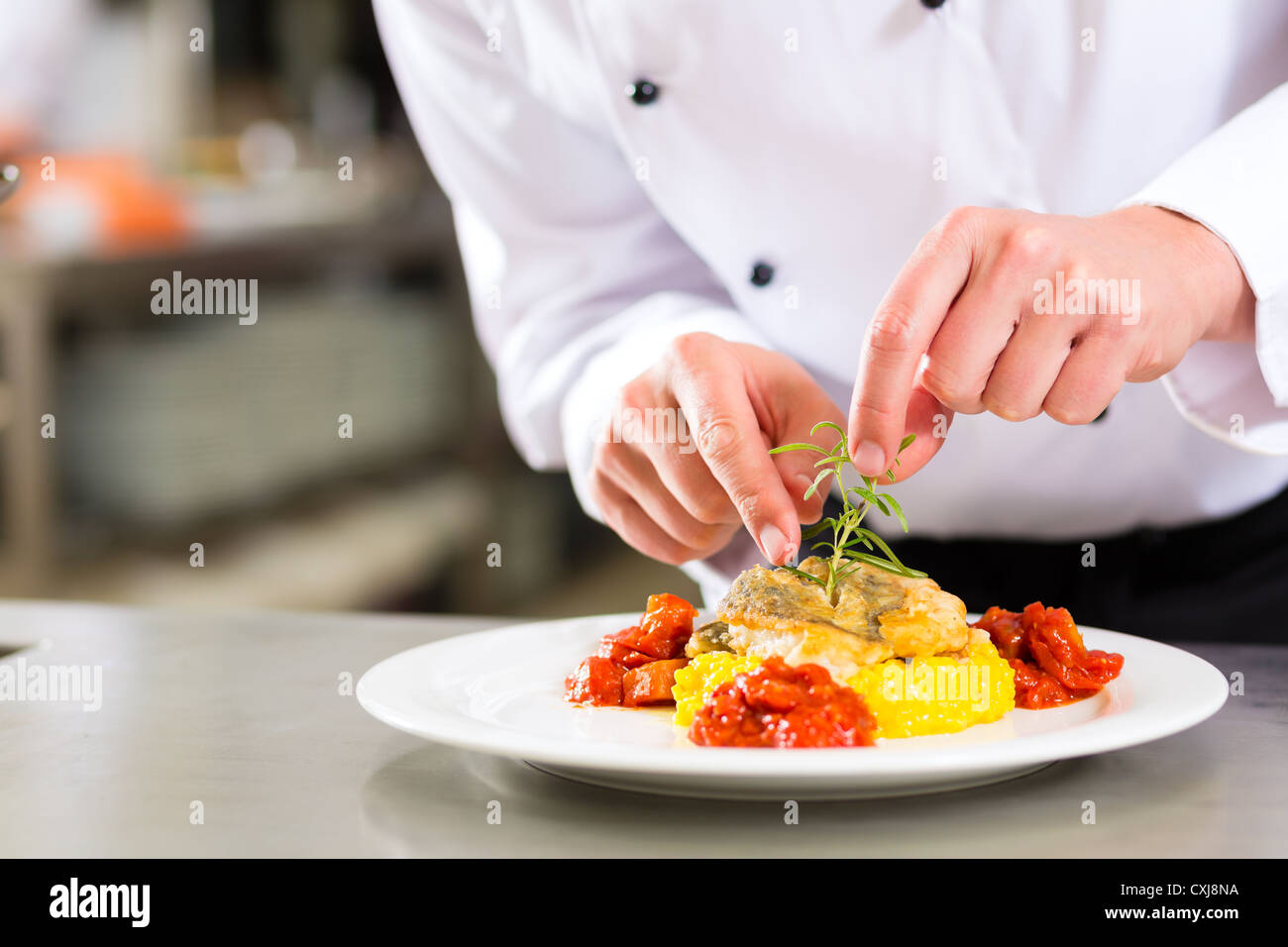 Chef in hotel or restaurant kitchen cooking, he is finishing a dish on ...