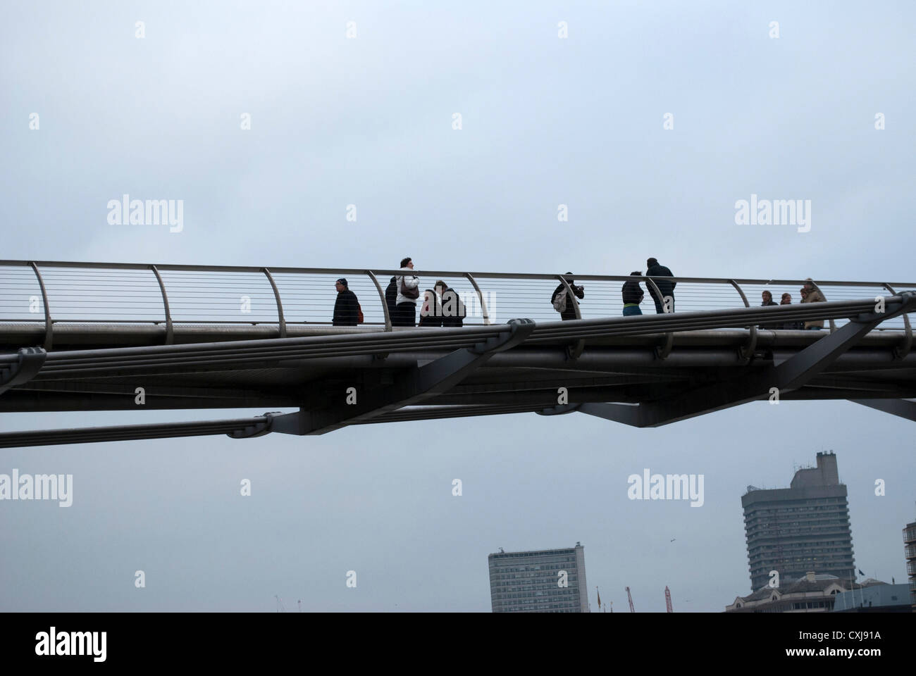 People walking over the The Millennium Bridge against a pale sky with ...