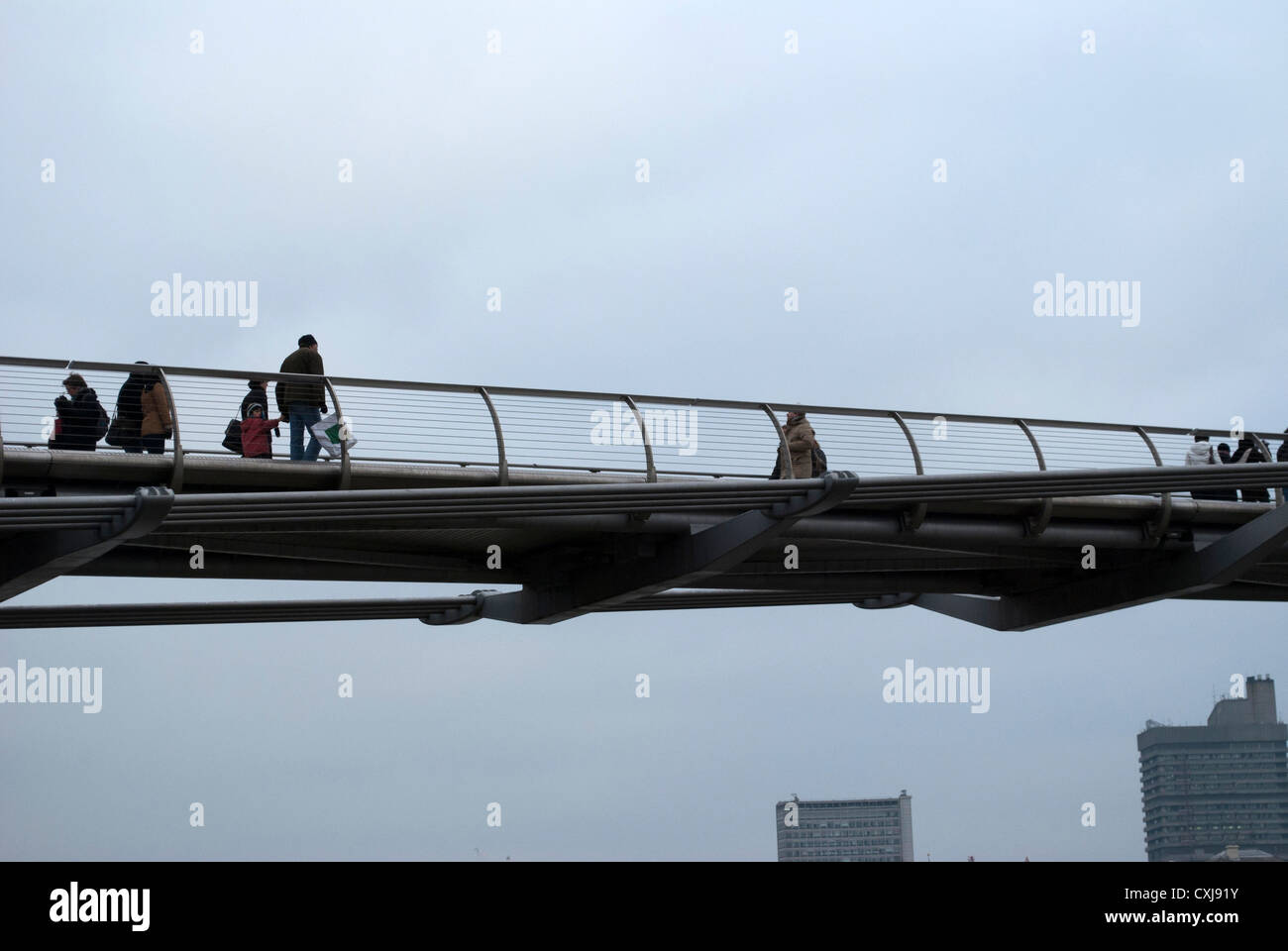 People walking over the The Millennium Bridge against a pale sky with ...