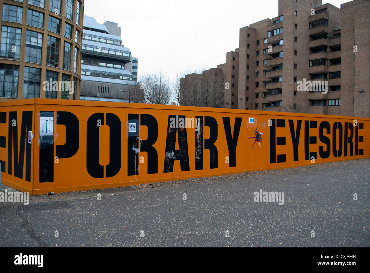 Black and yellow 'TEMPORARY EYESORE' sign on barrier around ...