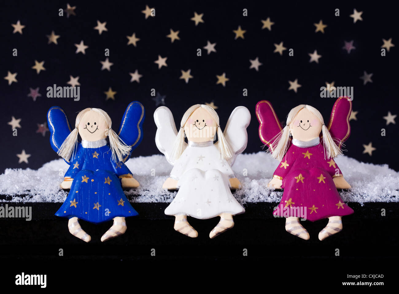 Three seated wooden angels in the snow against a starry black ...