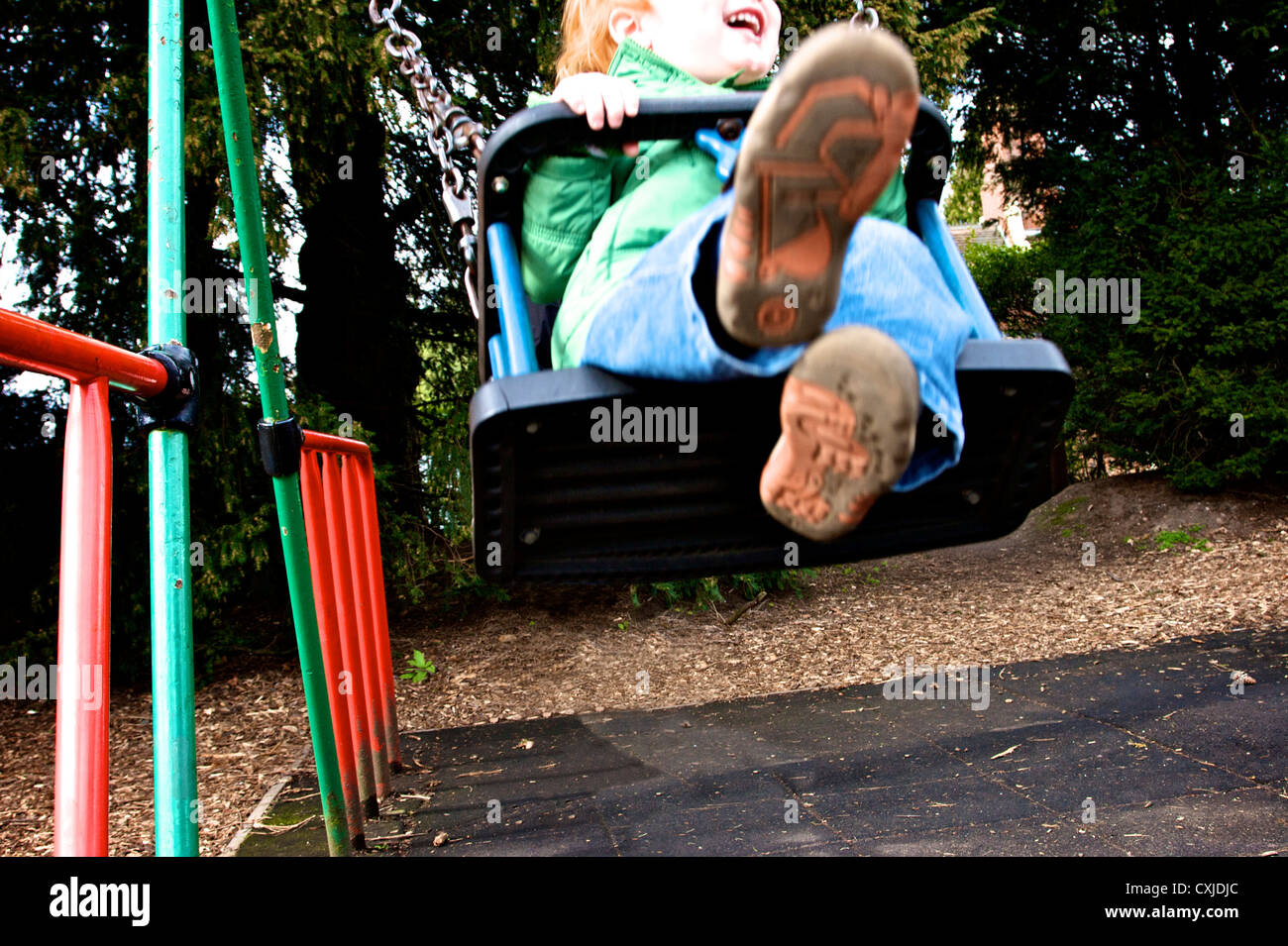 Young boy with red hair on swing looking straight at camera in park ...