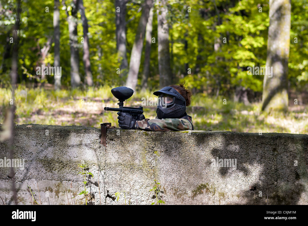 Paintball player shooting opponent from behind a wall during a ...