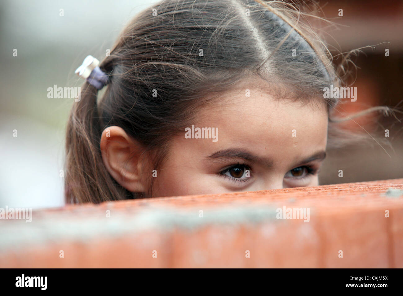 Girl peeking over a brick wall Stock Photo - Alamy