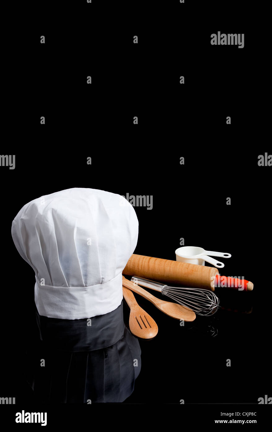 Chef's hat and various utensils on a black background with copy space ...