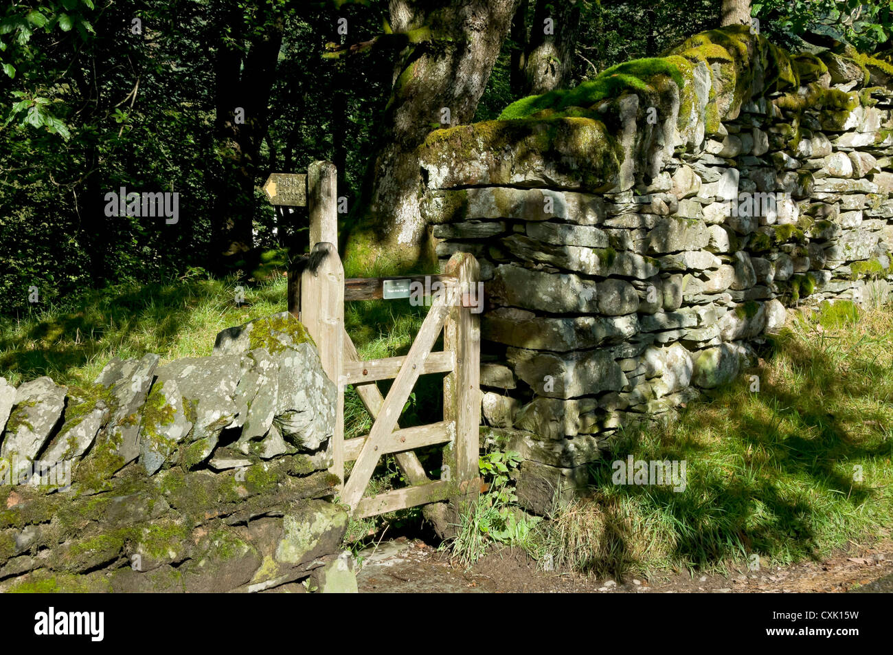Public footpath path with wooden gate set in dry stone wall in summer ...