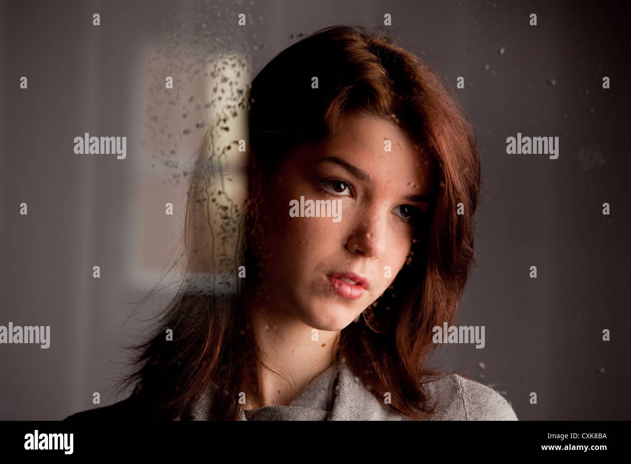 Young woman looking sadly through window glass Stock Photo - Alamy