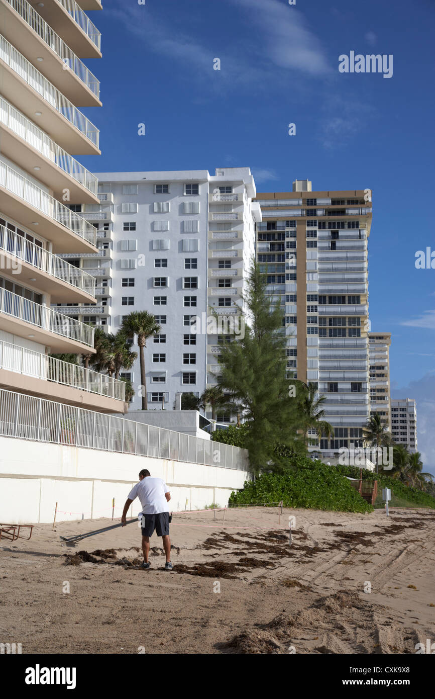 worker cleaning beach raking sand in front of apartments hotels and ...