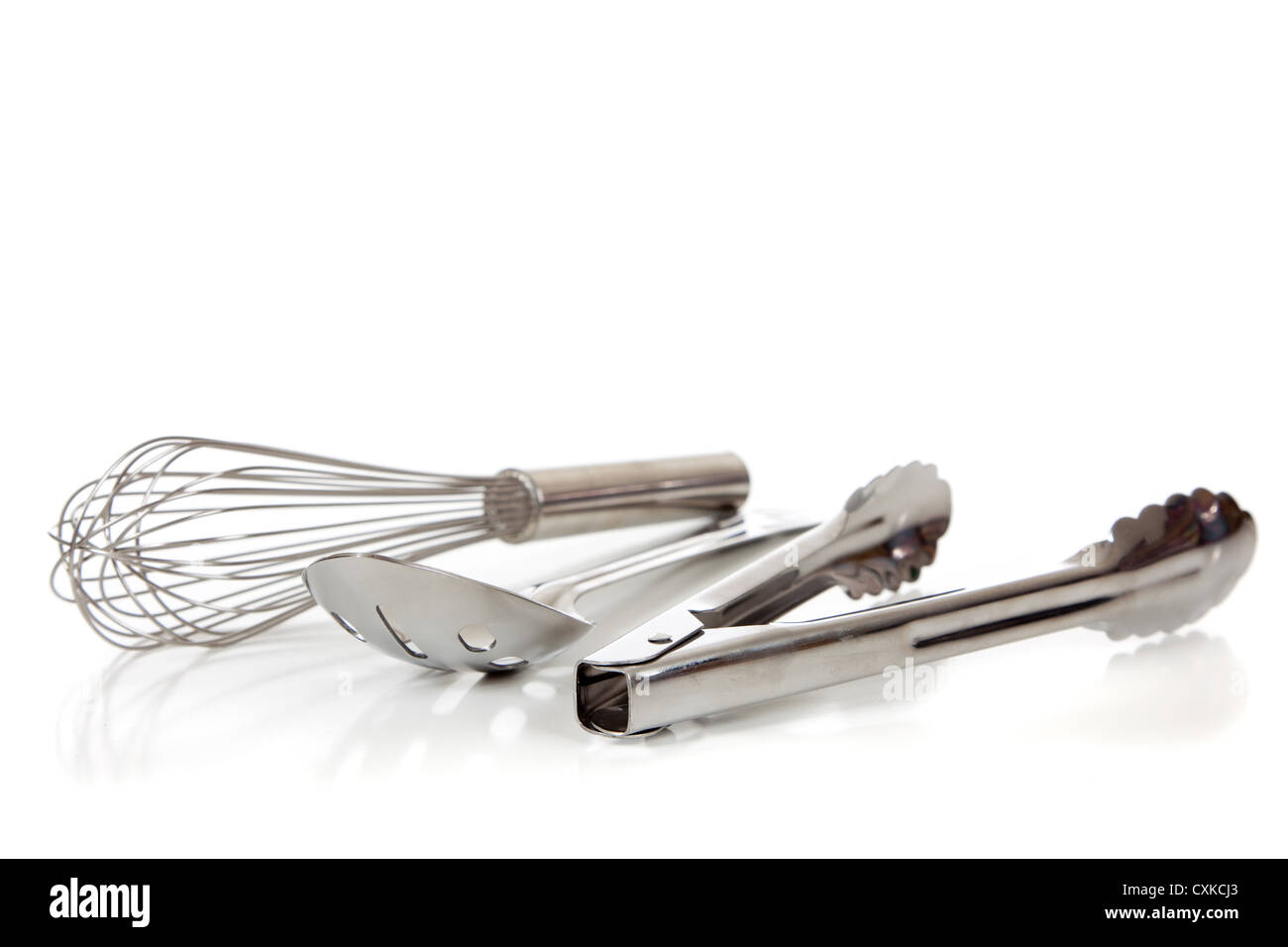 Silver kitchen utensils including whisk, tong and spoon on a white ...