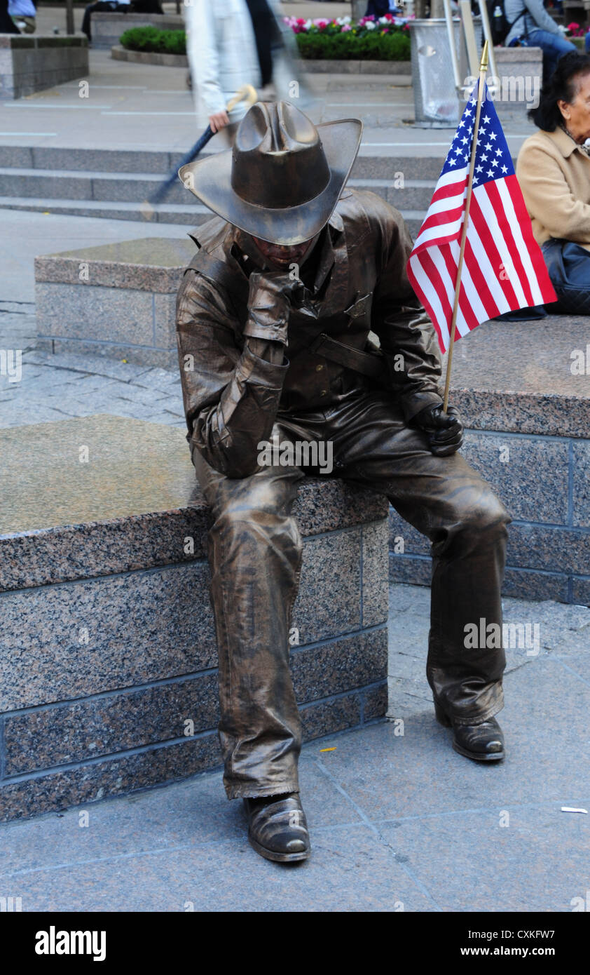 Cowboy mime artist, holding American Flag, sitting granite seat ...