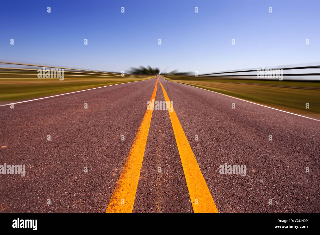 A long road bordered by farm fences and telephone wire against a blue ...