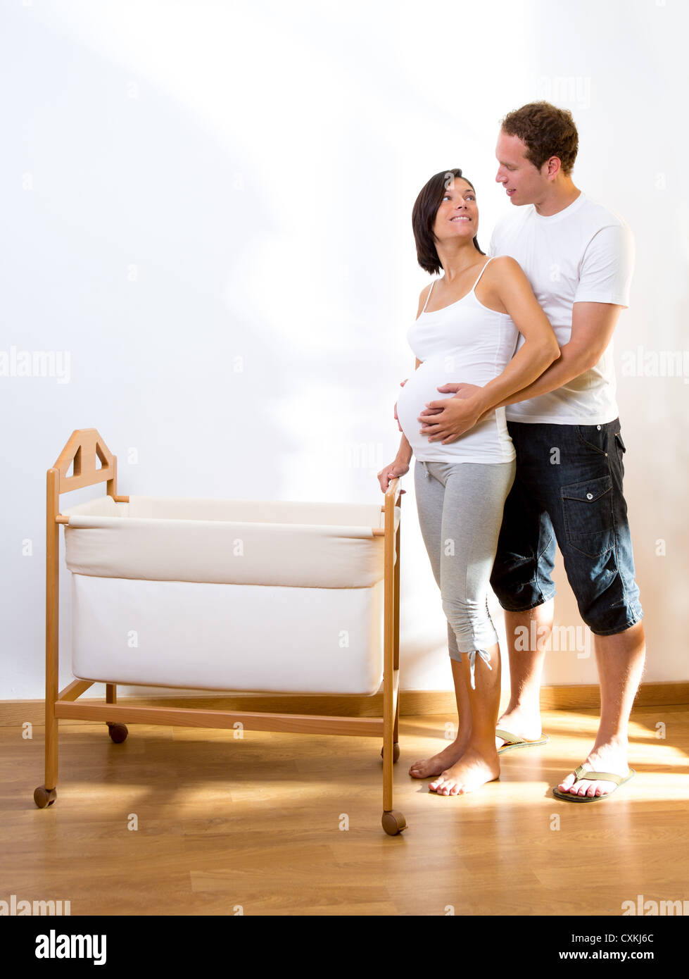 Couple with pregnant woman hug with baby cradle at home Stock Photo - Alamy