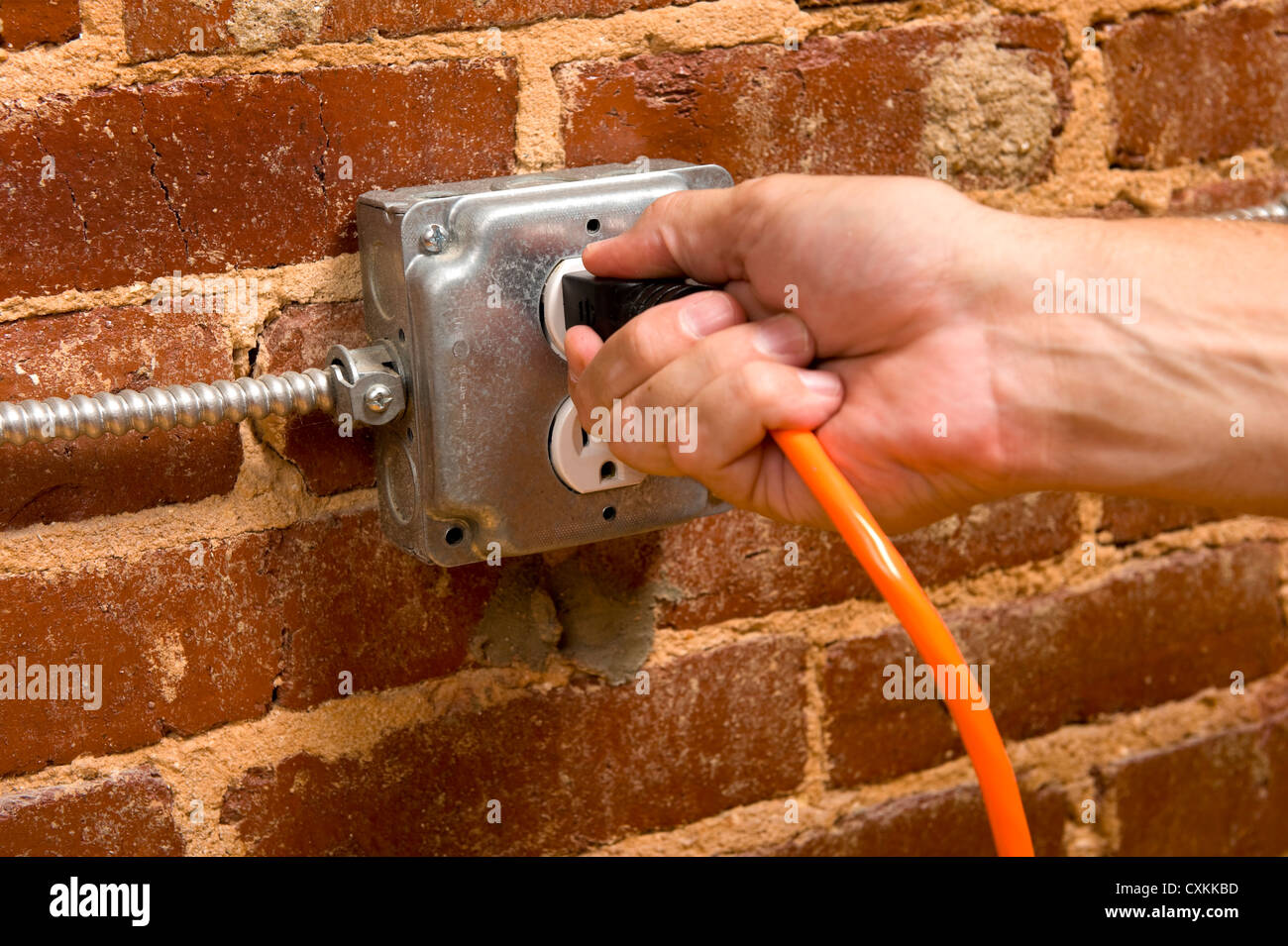 a man's hand plugging in an extension cord in a junction box electrical ...