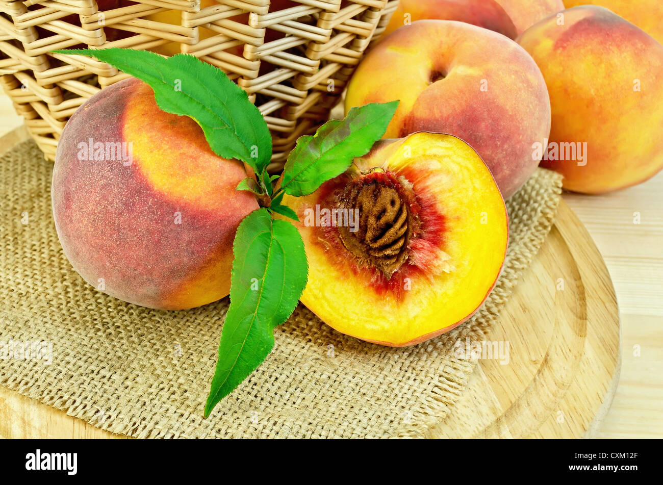 Several whole peaches, half peach, twig with green leaves, wicker ...
