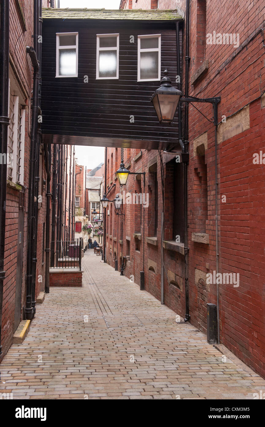 View down narrow enclosed alleyway, lined with high brick walls & glass ...