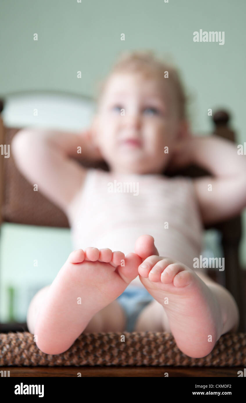 Little baby girl sitting on chair. Primary focus on feet Stock Photo ...