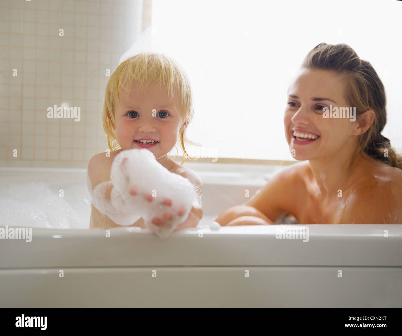 Baby playing with foam while taking bath with mother Stock Photo - Alamy