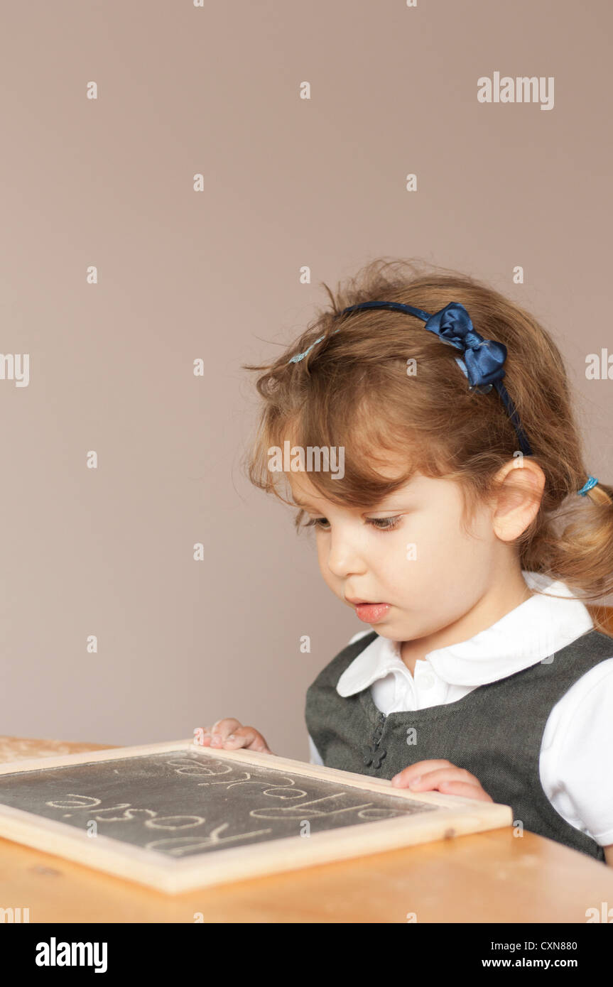 Four year old girl in school uniform practicing writing on a small ...