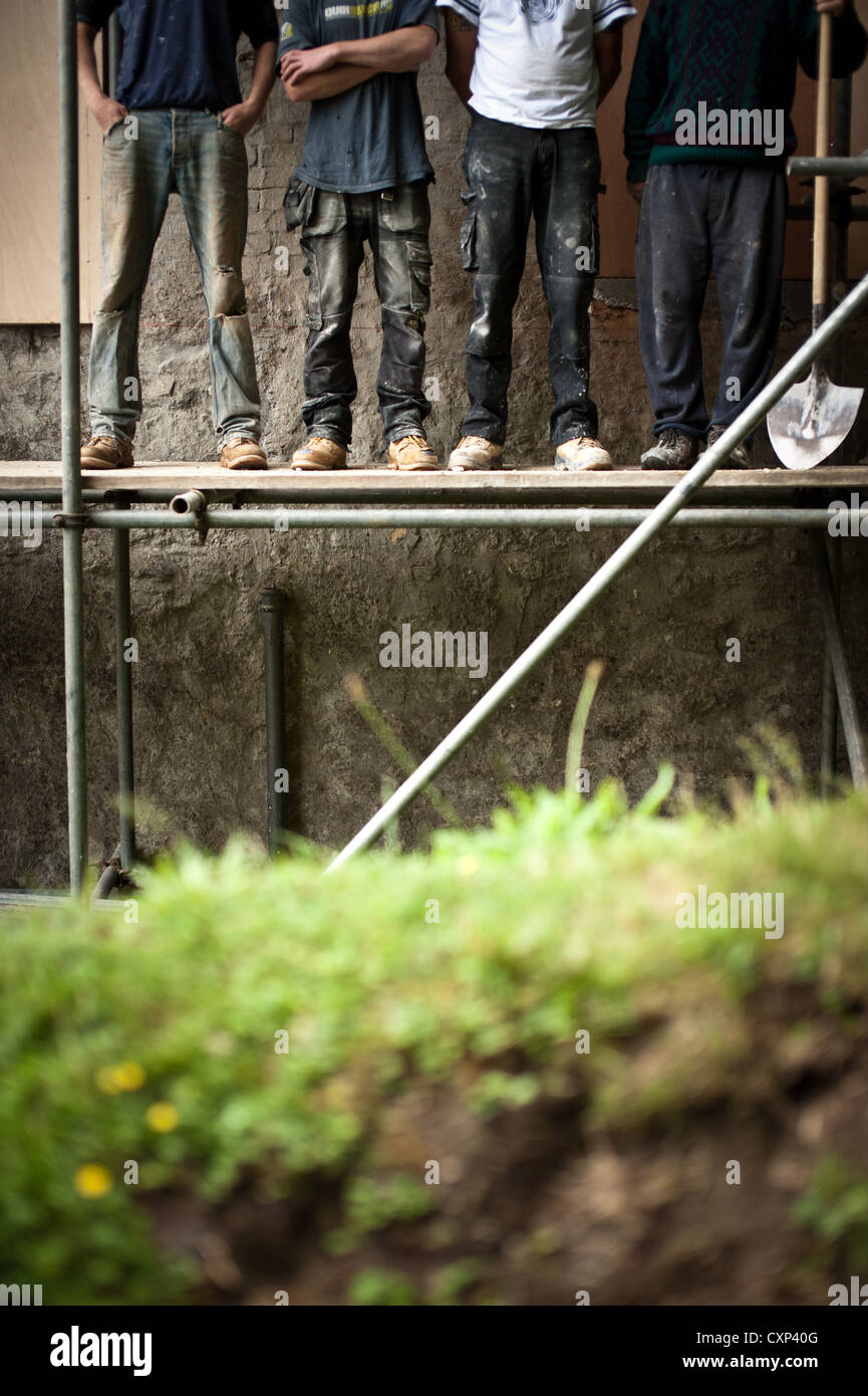 Four builders standing in a row on scaffolding wearing workwear ...