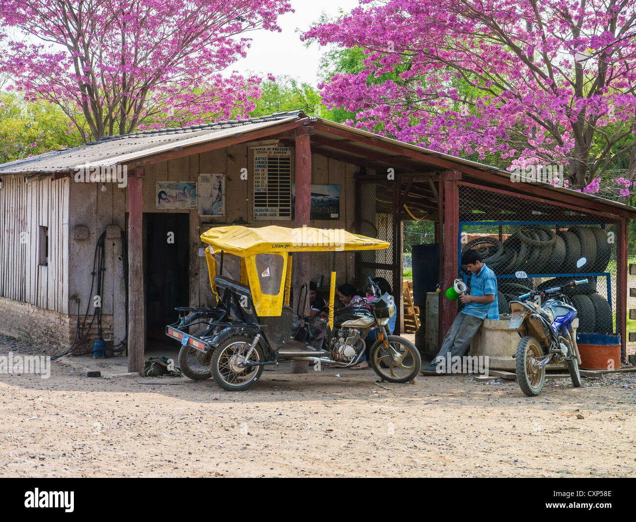 A man sits next to his motorcycle pedicab in front of a modest house in ...