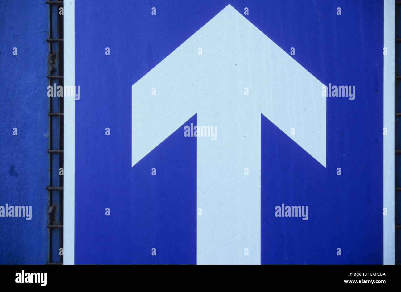 Detail of white direction arrow on blue roadsign mounted on wall ...