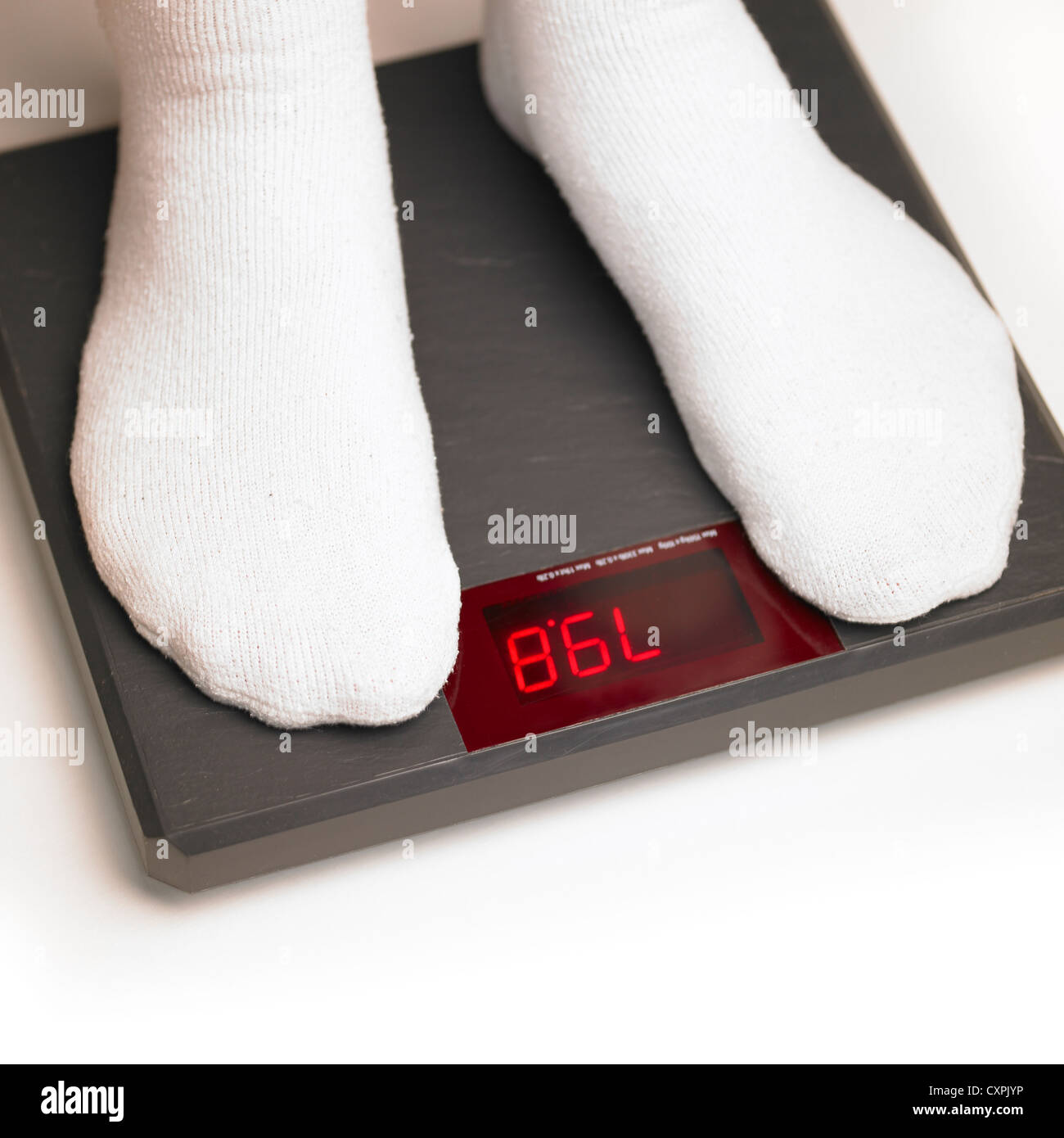 Feet wearing white sports socks standing on digital bathroom scales ...