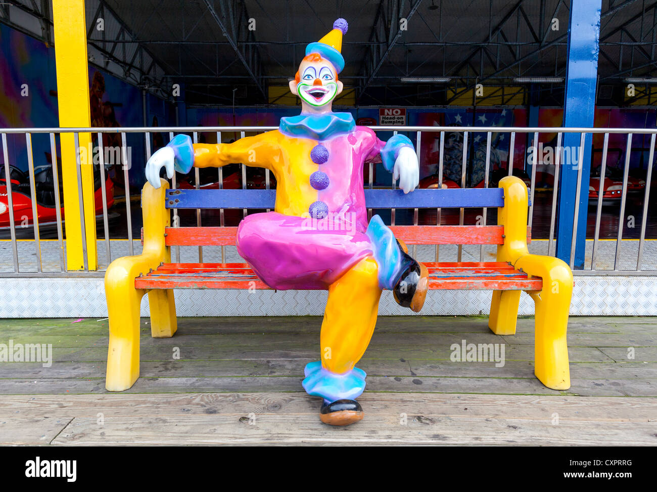A clown sits on a bench by a bumper car ride in an amusement park at ...