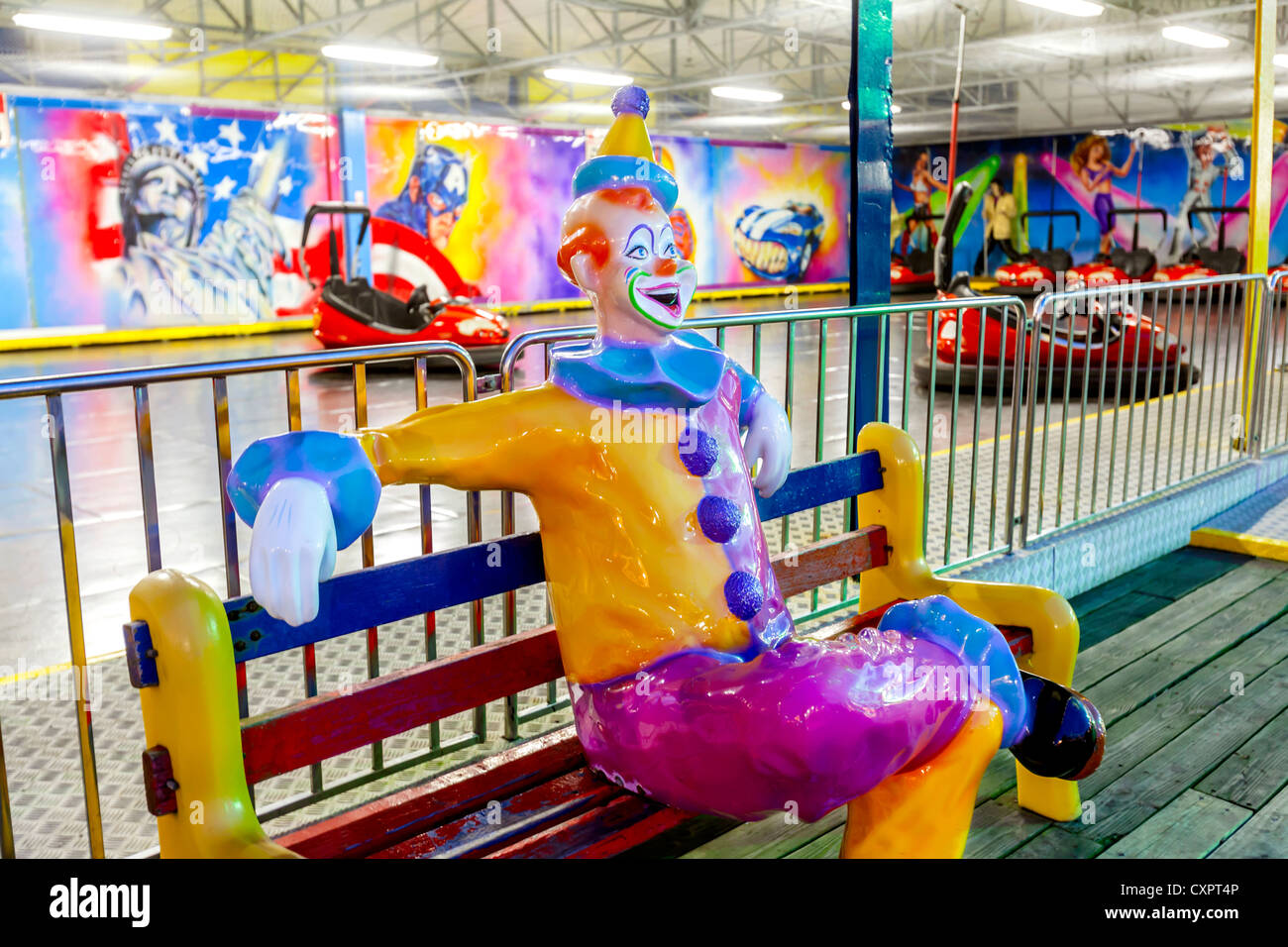 A clown sits on a bench by a bumper car ride in an amusement park at ...