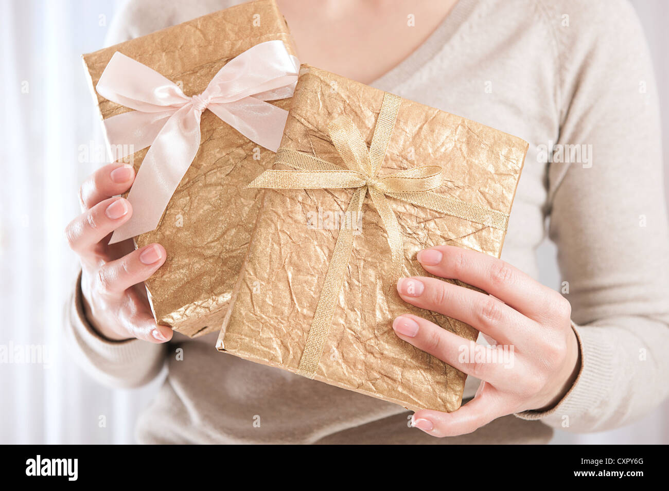 Young female holding a two boxes wrapped in golden paper with ribbon ...