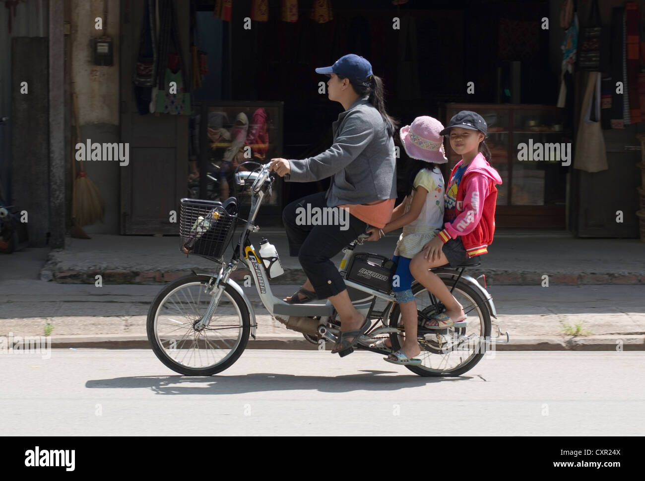 Two girls ride on the back seat of their mothers electric bicycle in ...