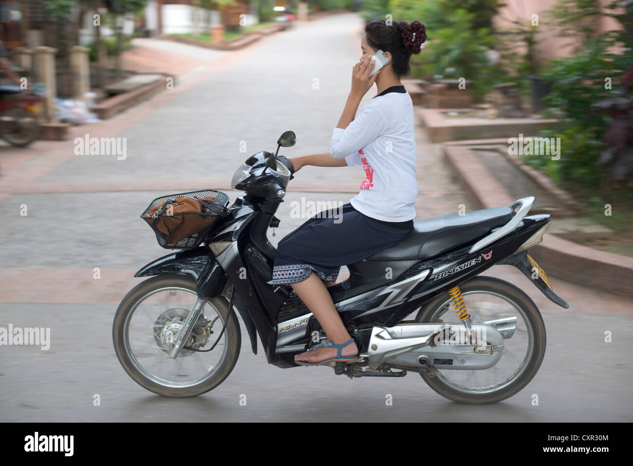 A young woman uses her mobile phone while driving her motorbike in ...
