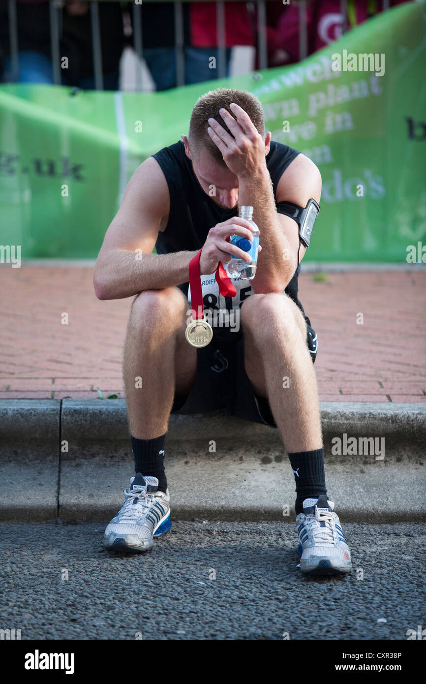 Runner exhausted after running half marathon sits on road holding their ...