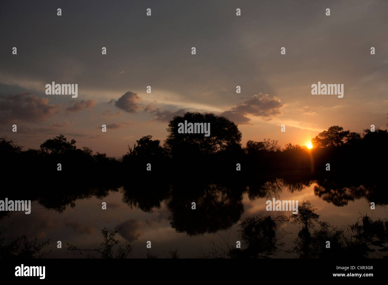 Red sunset over African water hole with reflection in water. Silhouette ...