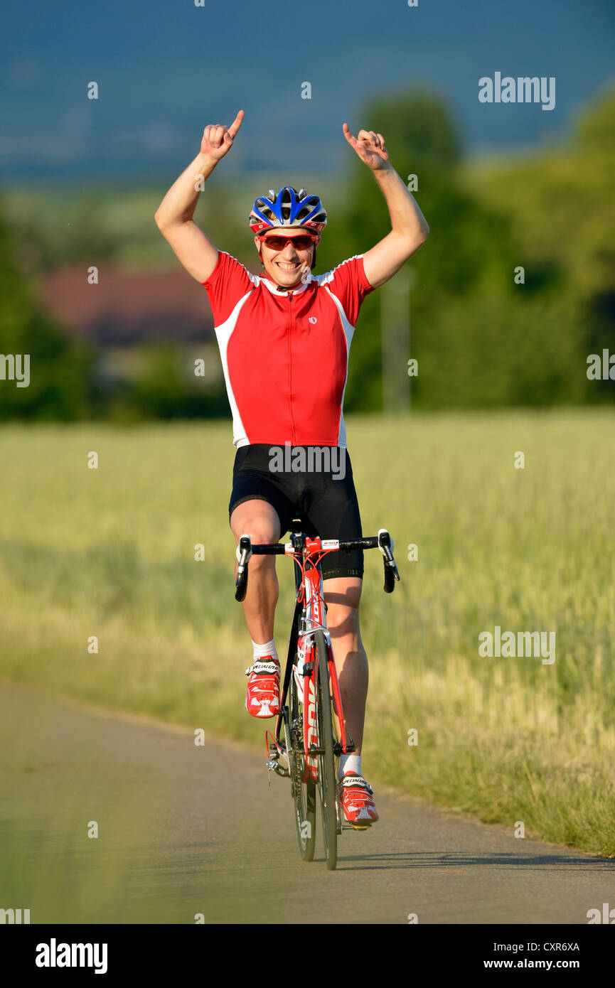 Racing cyclist riding a bicycle, arms raised in a victory pose ...
