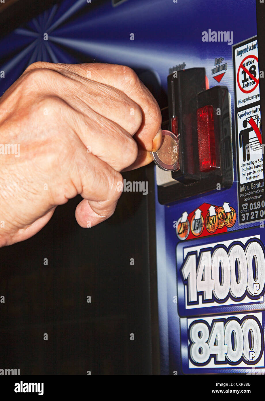 A man's hand is inserting a euro coin into a slot machine, warning sign ...
