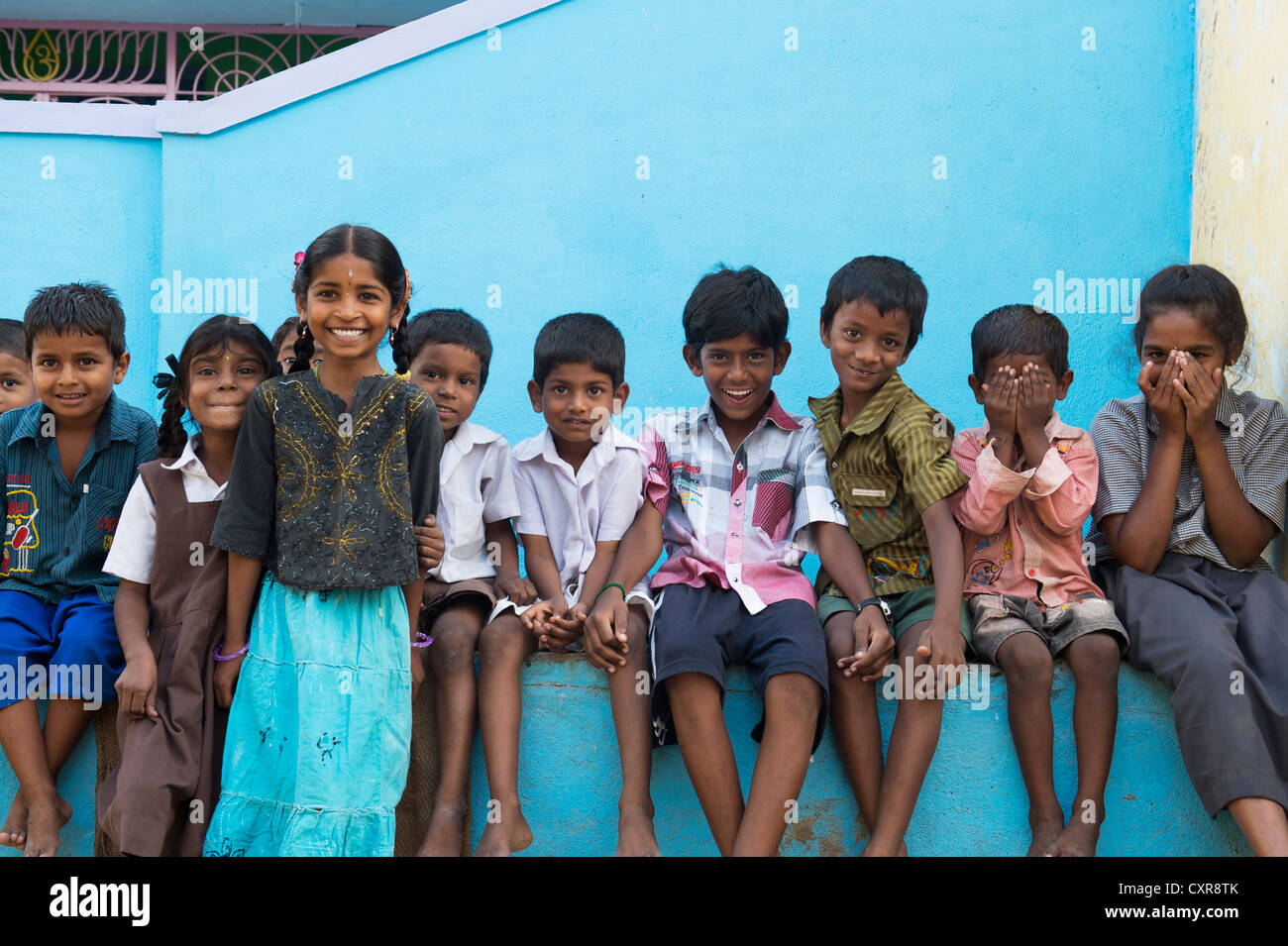 Happy young rural Indian village children sitting against a blue wall ...