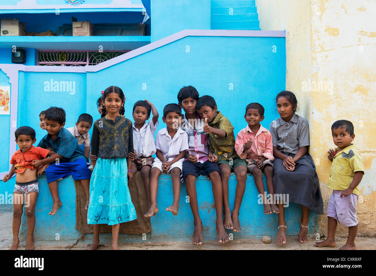 Happy young rural Indian village children sitting against a blue wall ...