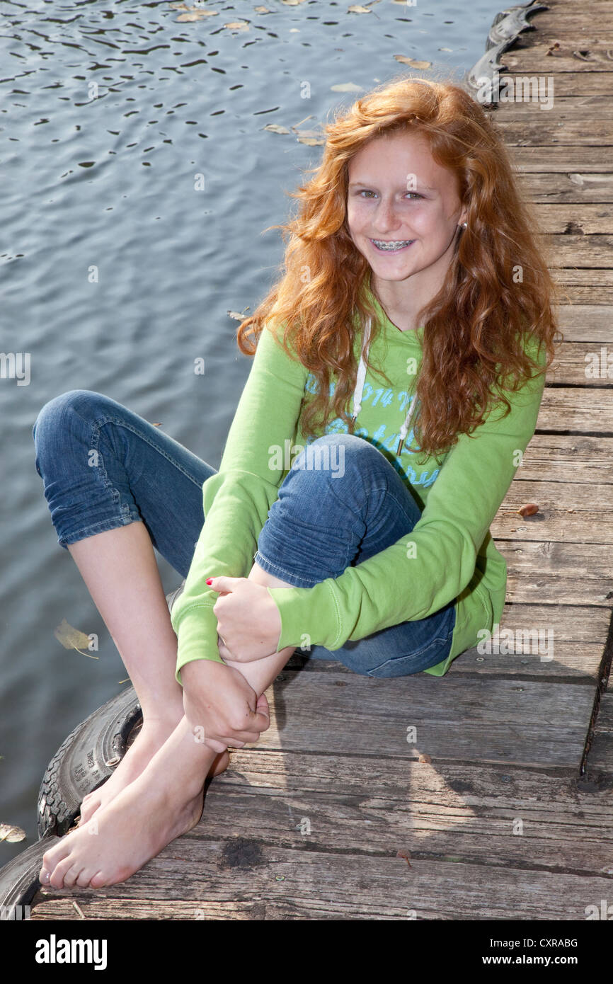Red-haired girl with braces sitting on a jetty Stock Photo - Alamy