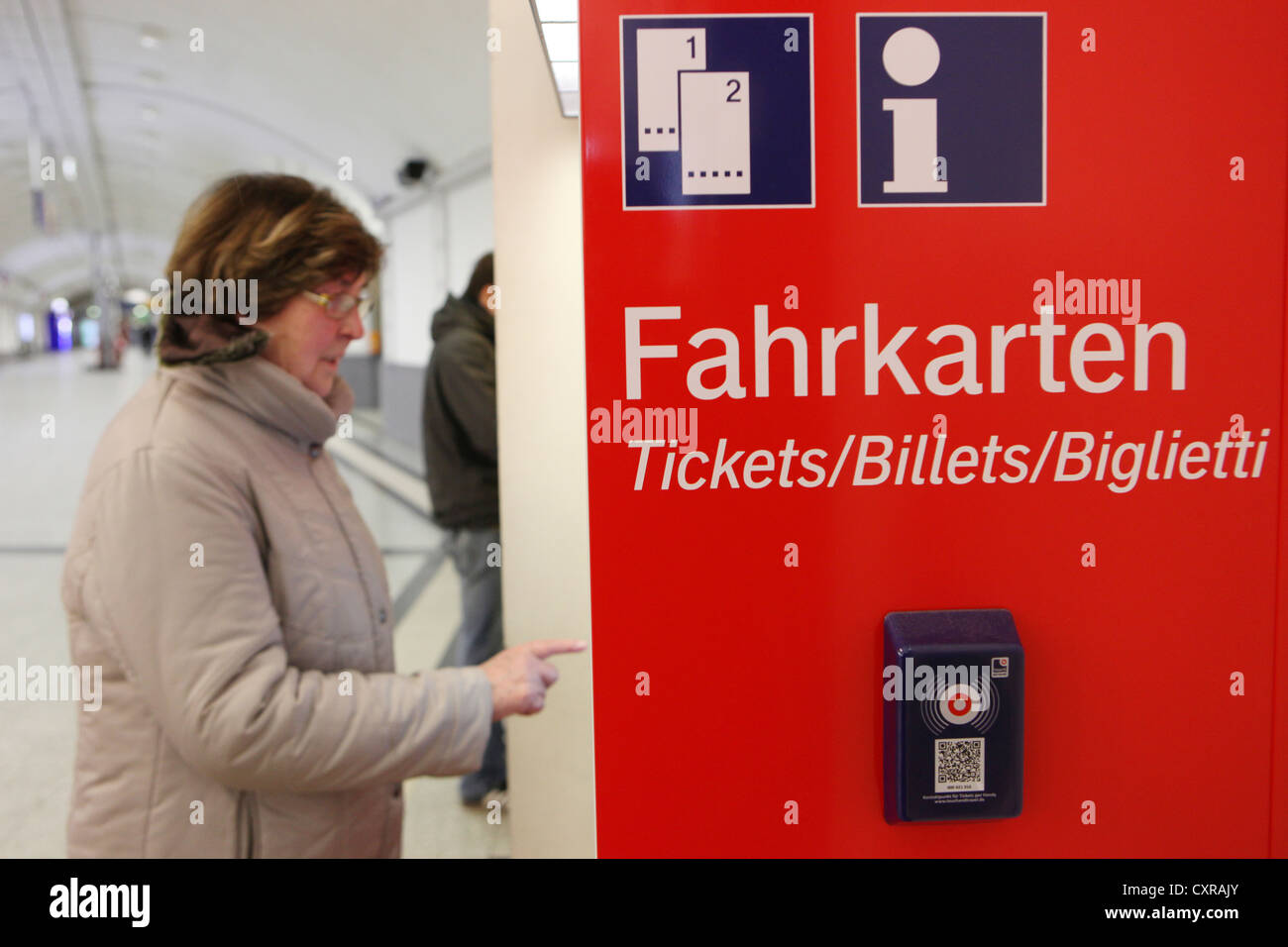 Elderly woman getting a ticket from a ticket machine at a railway ...